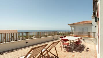 Terraço com mesa e cadeiras, com vista para um corpo de água.