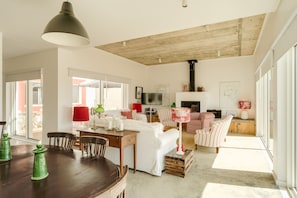 Uma sala de estar ampla com teto alto, mesa de jantar e lareira.