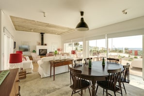 Uma sala de estar ampla com uma grande mesa de jantar, assentos confortáveis e vista para o exterior.