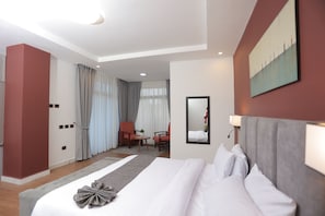 Quarto de hotel com cama, cadeira, escrivaninha e um quadro na parede.
