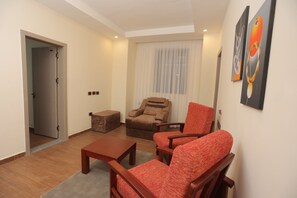 Uma sala de estar com sofá, poltrona, banquinho e mesa de centro de madeira.