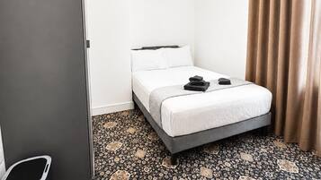 Quarto de hotel com cama, guarda-roupa, lixeira e carpete estampado.