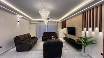 Uma sala de estar moderna com um candelabro, dois sofás, uma mesa de centro, uma TV e uma planta.