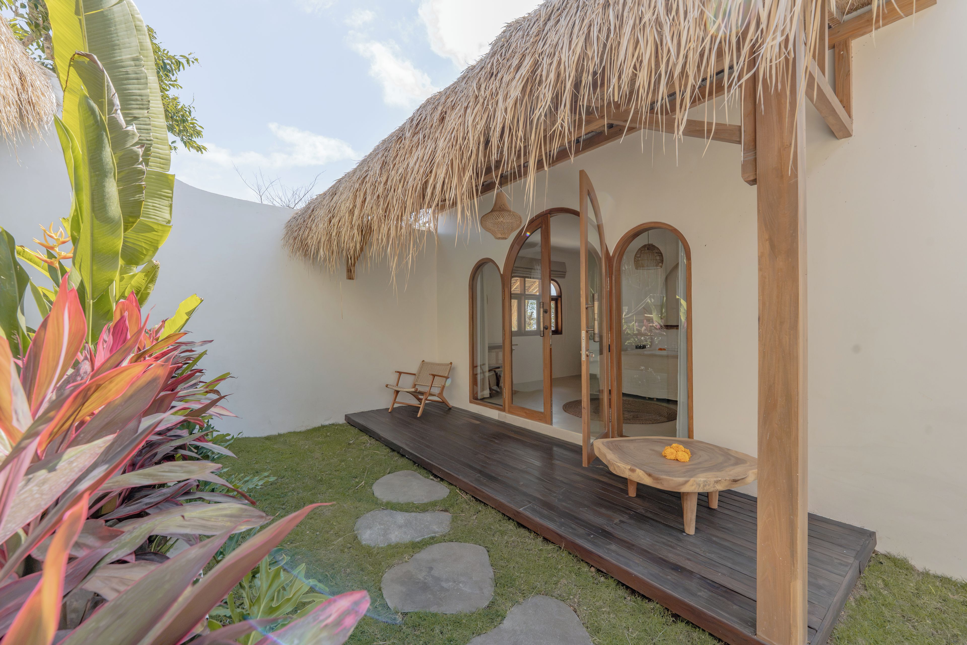 Uma área externa moderna com deck de madeira, estrutura de telhado de palha e espaço de estar com mesa e cadeiras.