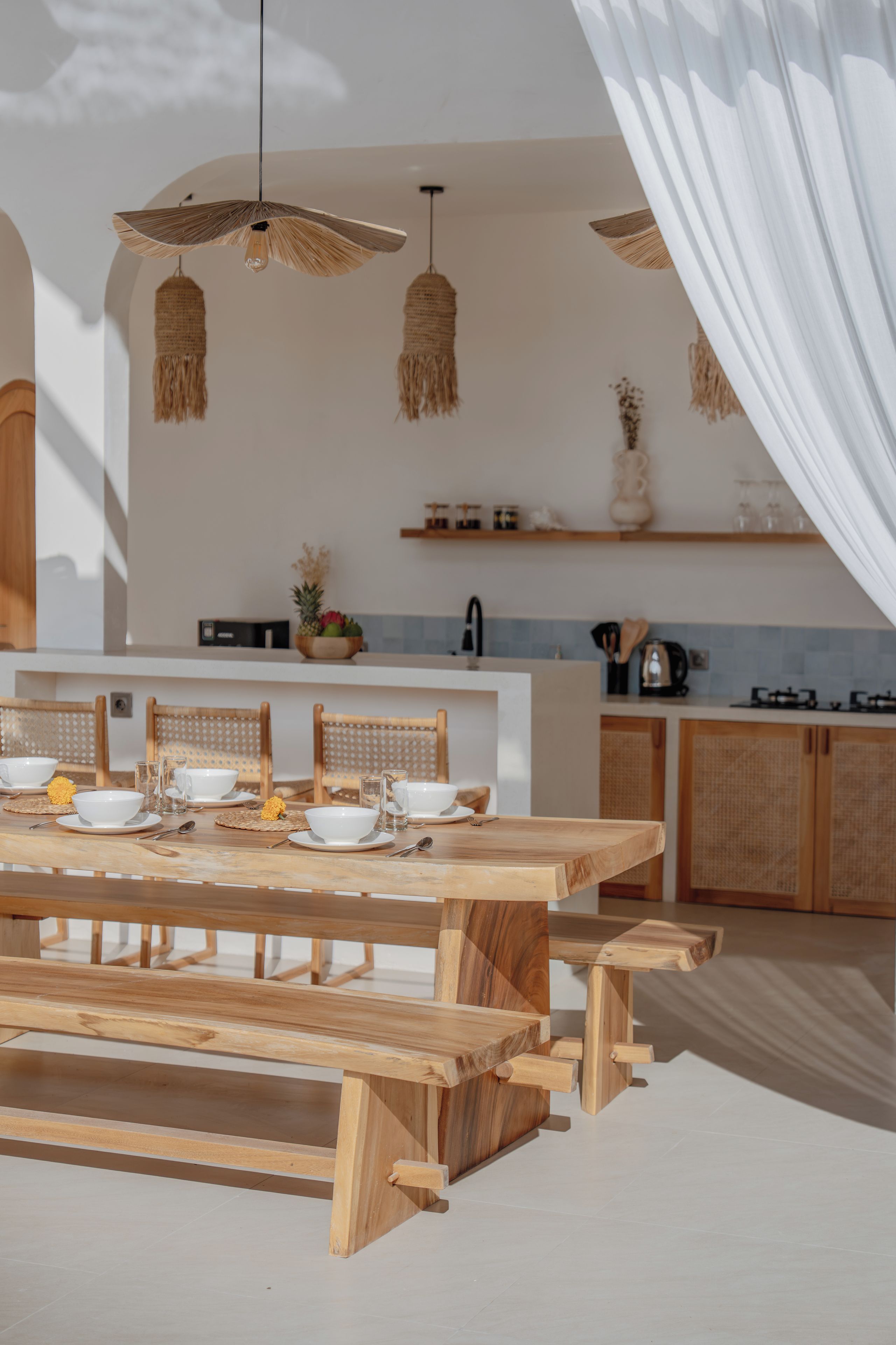Cozinha moderna com mesa de jantar de madeira para quatro pessoas, luminária pendente e ilha central com fogão embutido.