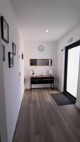 Um corredor com piso de madeira, um console preto com espelho, quadros na parede e uma porta que dá para outro quarto.