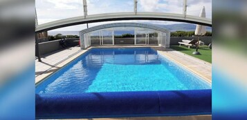 Piscina com estrutura de vidro, cercada por um terraço com espreguiçadeiras e vista para a paisagem.