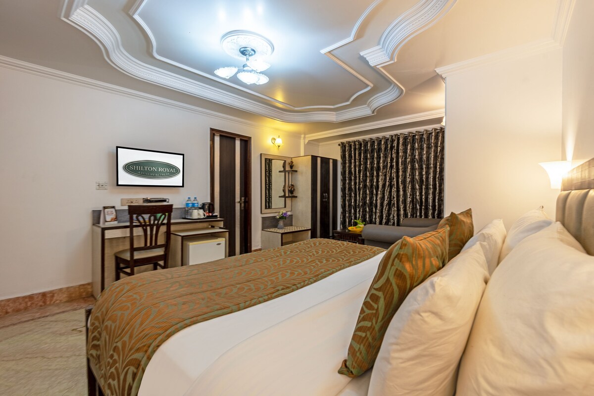 Quarto de hotel com cama, escrivaninha, cadeira e luminária no teto.