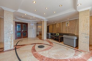 Um hall de entrada com piso de mármore, balcão de recepção, sofá e uma porta com a inscrição 'RECREAÇÃO'.