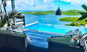 Uma área de estar junto à piscina, com vista para uma marina e vegetação.