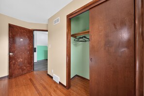 Um corredor com piso de madeira, um armário com cabides e uma porta que dá para outro cômodo.