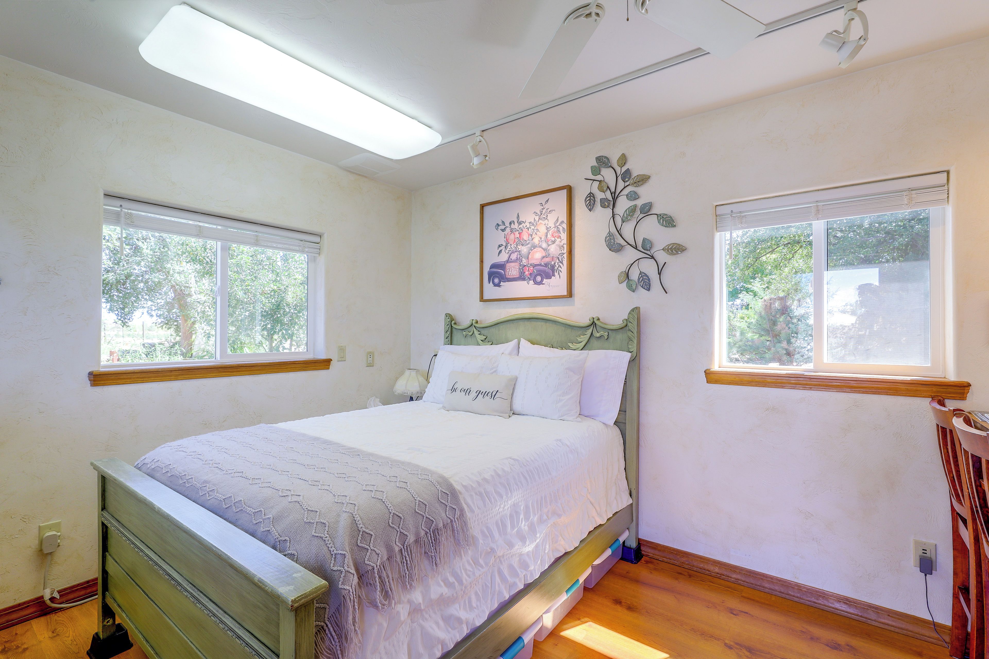 Quarto com cama, duas janelas, um quadro na parede e um radiador.