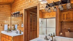 Interior de uma cabana de madeira com banheiro que inclui duas pias, armários de madeira e um espelho.