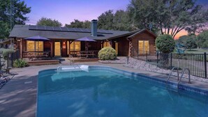 Uma cabana de toras com piscina, área de estar externa e vista para as árvores ao redor.