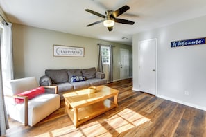 Uma sala de estar com sofá, mesa de centro, ventilador de teto e um letreiro com a palavra 'Welcome' na parede.