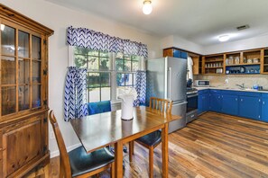 Cozinha com mesa, cadeiras, geladeira, armários e janela com cortinas.