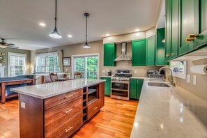 Cozinha moderna com ilha central, armários verdes e uma grande janela.