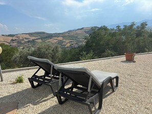 Duas cadeiras de descanso ao ar livre sobre um piso de cascalho, com vista para colinas ondulantes e céu claro.