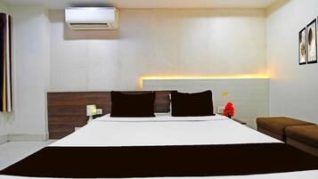 Quarto de hotel com cama, mesa de cabeceira, luminária e ar condicionado.