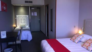 Quarto de hotel com cama, escrivaninha, cadeira, lixeira e porta.