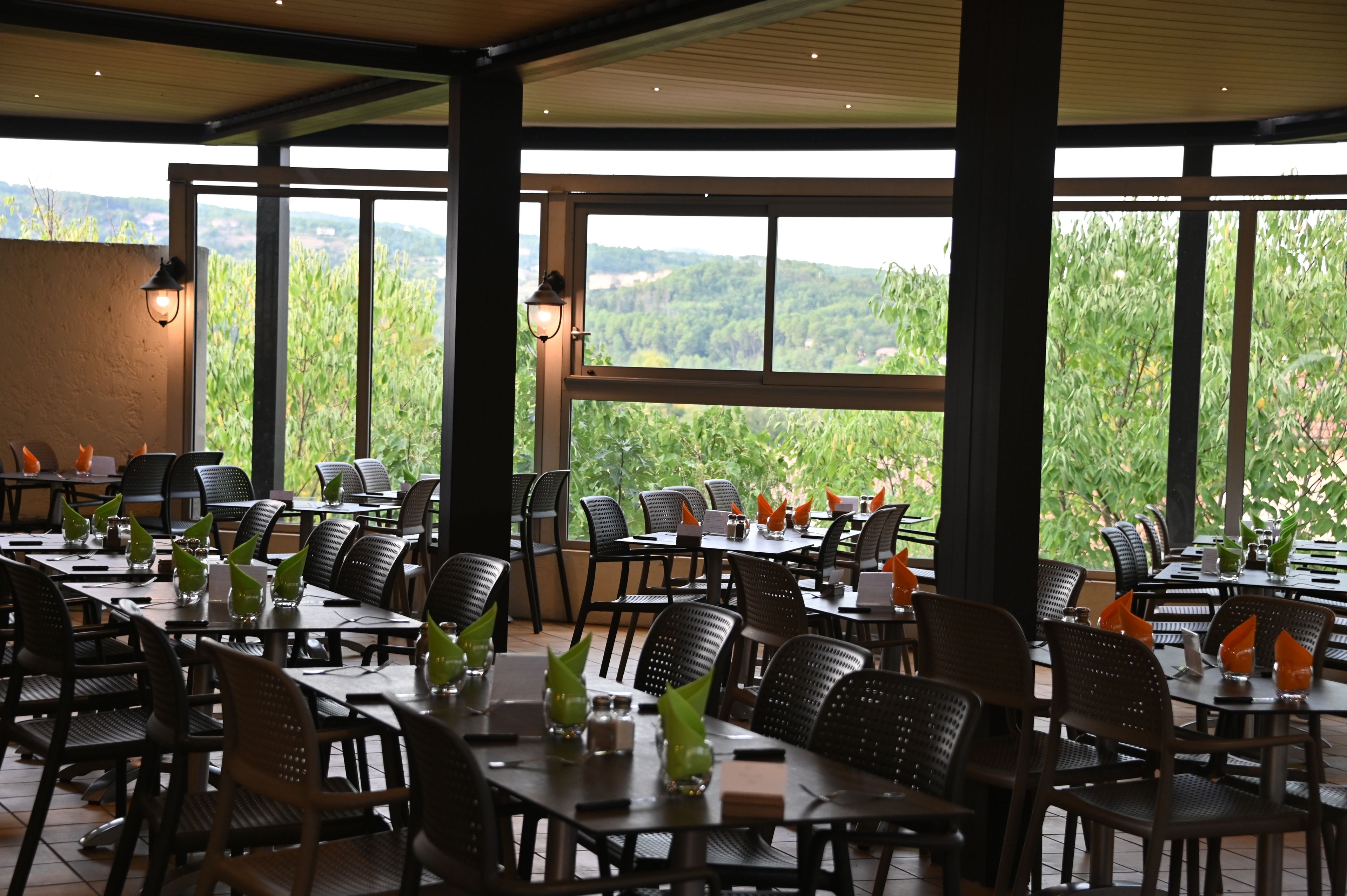 Restaurante com área externa, mesas e cadeiras, e vista para o verde.