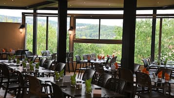 Restaurante com área externa, mesas e cadeiras, e vista para o verde.