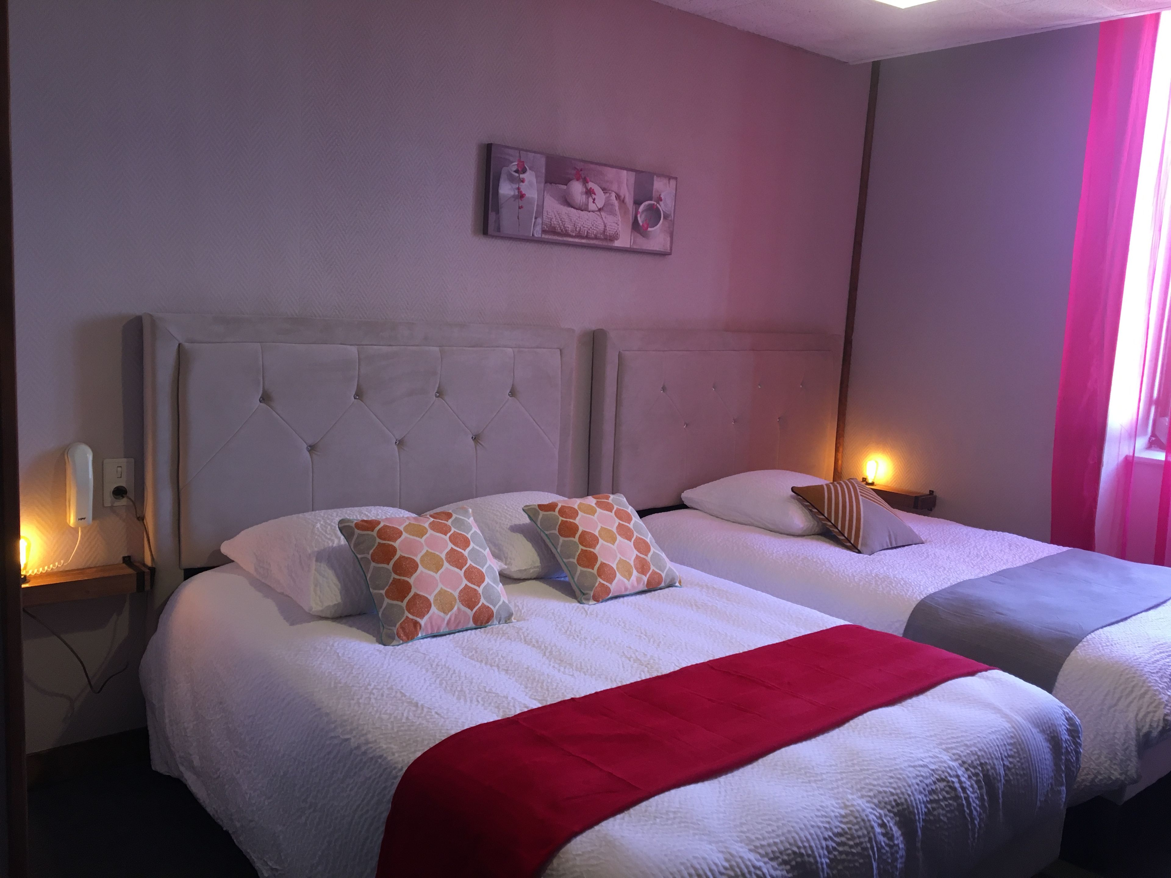 Quarto de hotel com duas camas, cabeceira estofada, um quadro na parede e abajur.