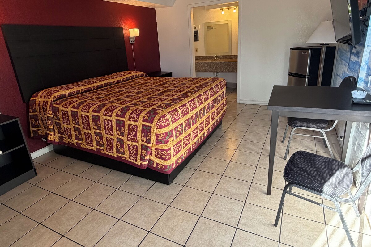 Quarto de hotel com cama, escrivaninha, cadeira e televisão.