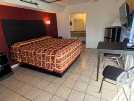 Quarto de hotel com cama, escrivaninha, cadeira e televisão.