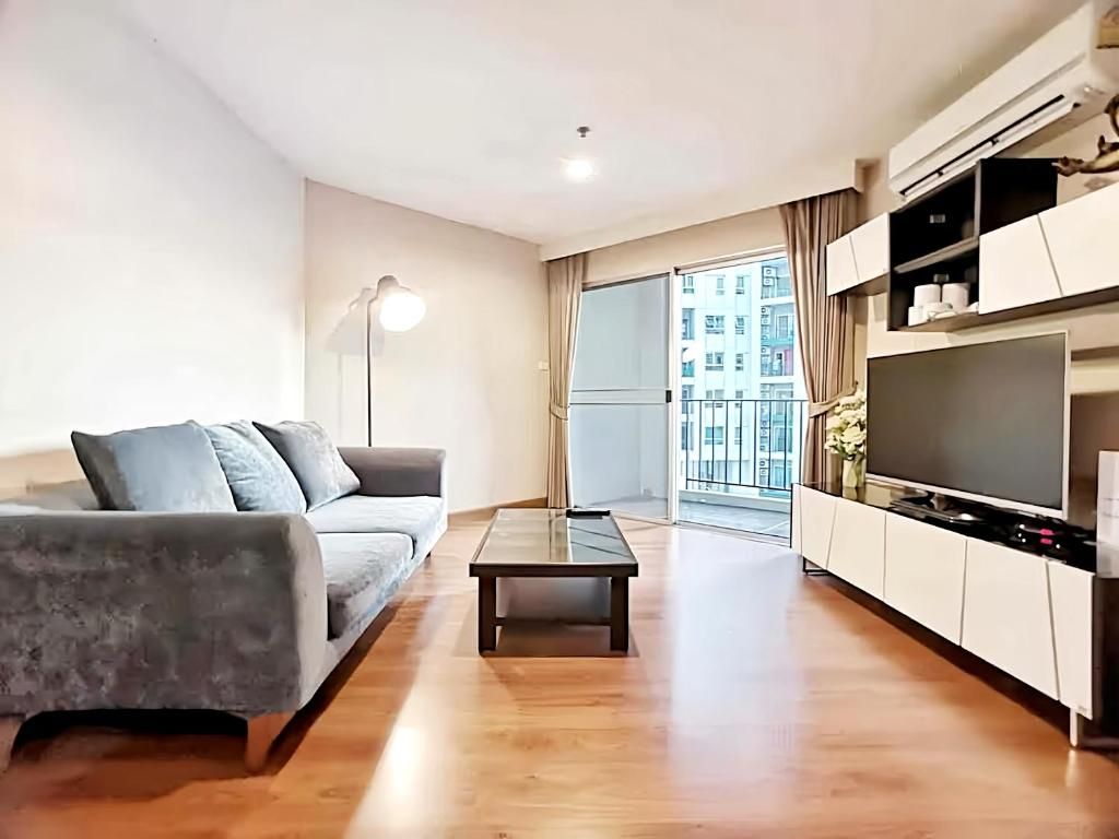 Uma sala de estar moderna com sofá, mesa de centro, televisão de tela plana e varanda com vista para edifícios.