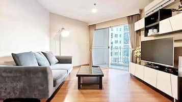 Uma sala de estar moderna com sofá, mesa de centro, televisão de tela plana e varanda com vista para edifícios.
