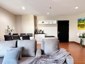 Uma sala de estar moderna com sofá, mesa de jantar com cadeiras, cozinha e uma porta.