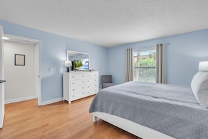 Quarto com cama, penteadeira, televisão e janela com cortinas.