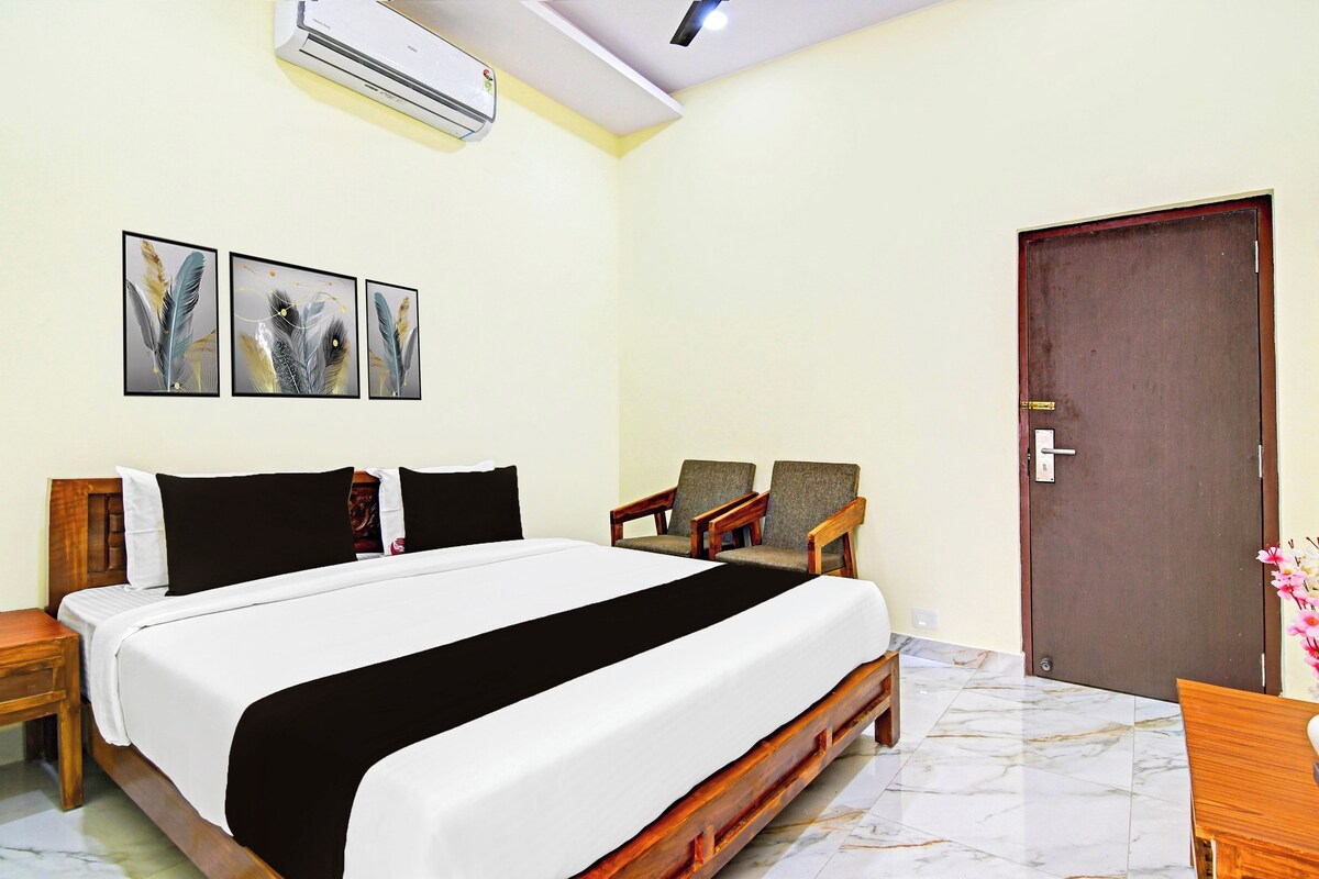 Quarto de hotel com uma cama, duas cadeiras, aparelho de ar condicionado e uma porta.