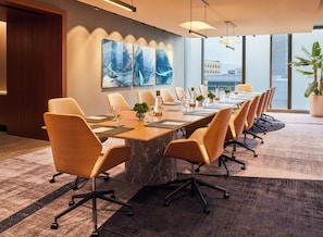 Sala de conferência com uma mesa comprida, cadeiras e vista para a cidade.