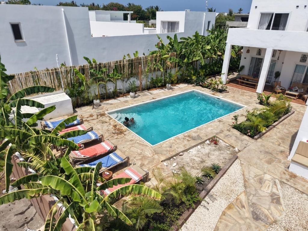 Piscina com espreguiçadeiras, cercada por um edifício branco com vista para o mar.