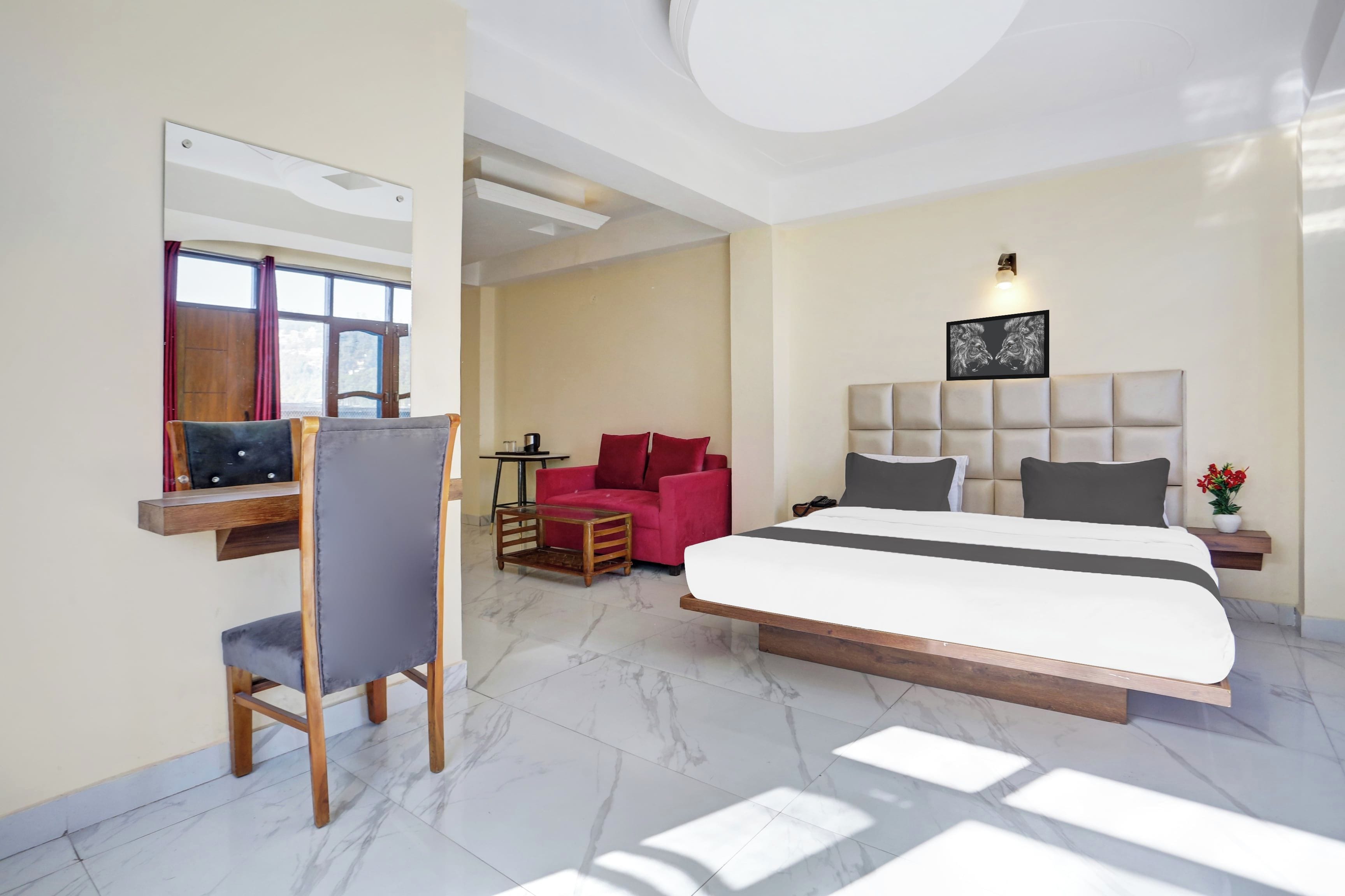 Quarto de hotel moderno com cama grande, escrivaninha com cadeira, sofá vermelho e pequena mesa.