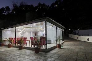 Estrutura envidraçada com piso de azulejos, área de estar e plantas em vasos.