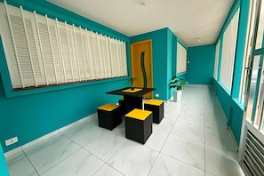 Corredor com paredes verde-água, uma mesa preta e amarela, e um vaso com planta.