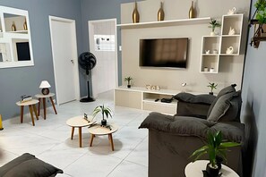 Uma sala de estar moderna com um sofá cinza, uma TV de tela plana e uma mesa de centro.