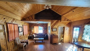 Interior de uma cabana de madeira com quarto no mezanino, área de jantar e sala de estar.