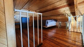 Interior de uma cabana de madeira com beliche, uma pequena escrivaninha e uma janela.