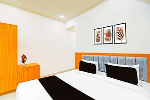Quarto com cama, guarda-roupa de madeira e mesa de cabeceira com um vaso de flores.
