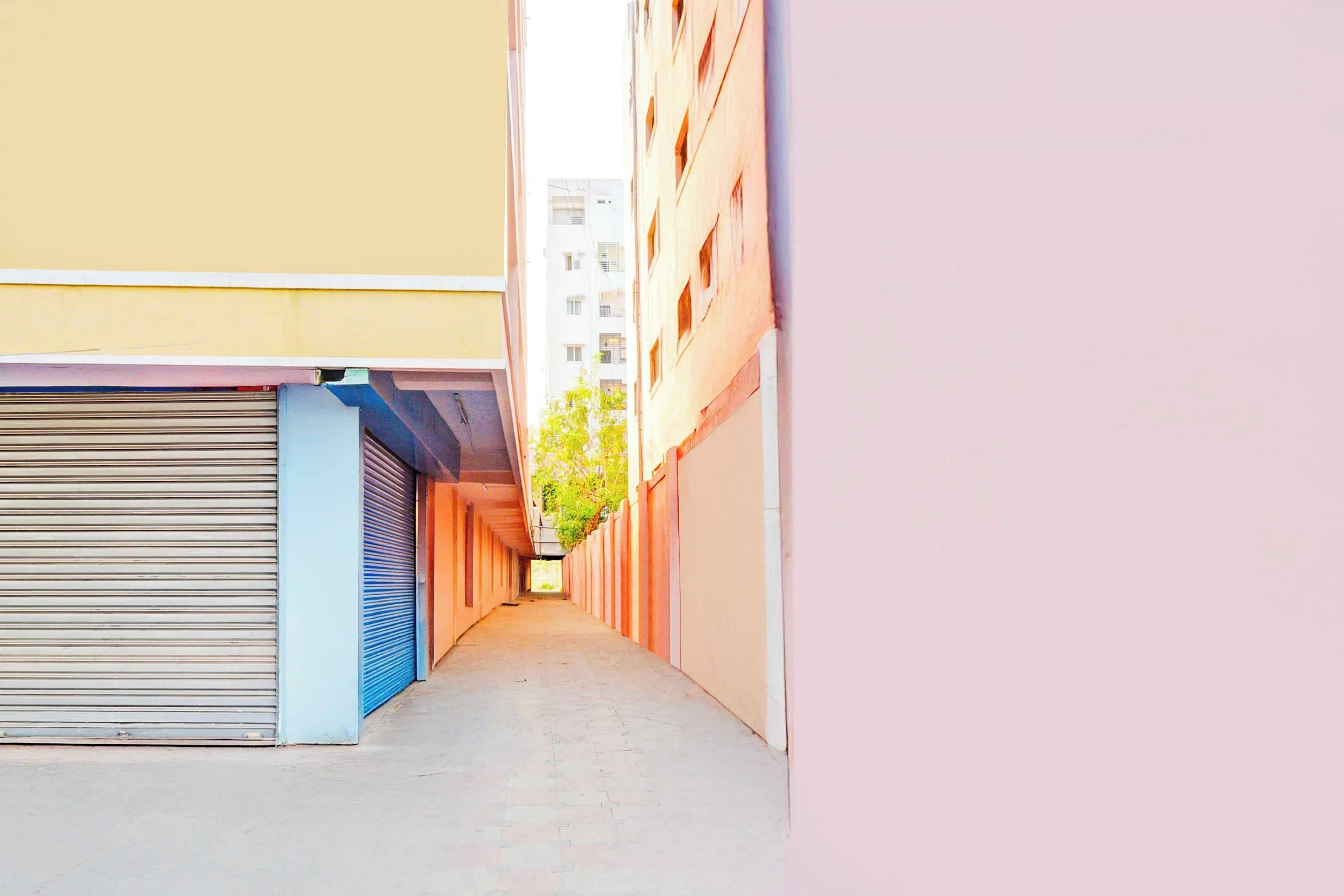 Um beco estreito entre edifícios, com persianas fechadas à esquerda e uma árvore ao centro.