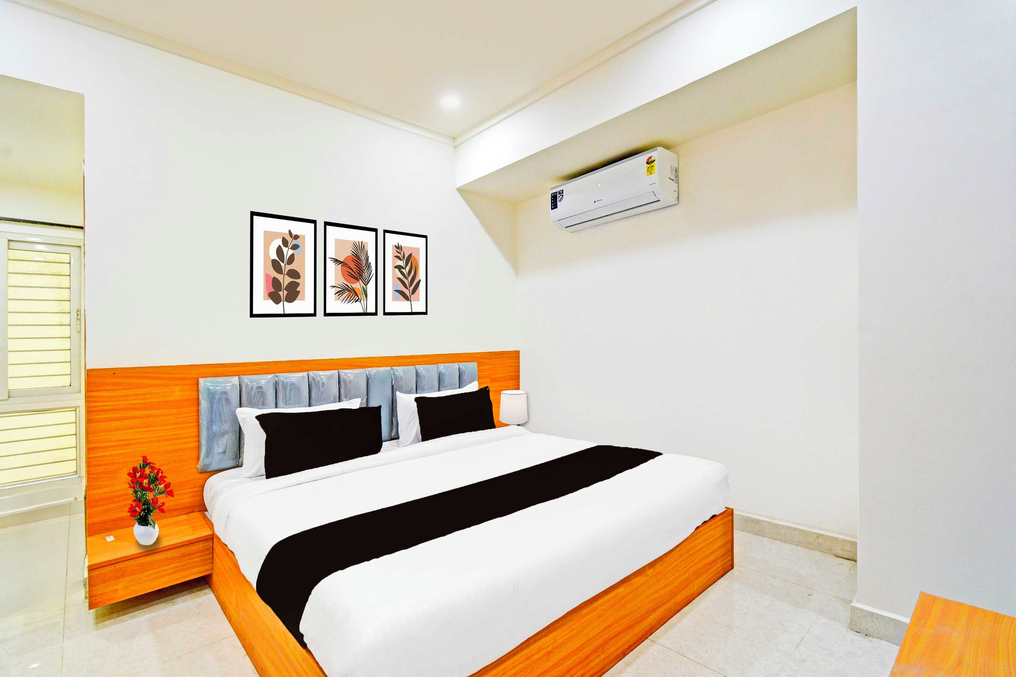 Quarto moderno com cabeceira de madeira, cama grande com roupa de cama preta e branca, mesa de cabeceira com um vaso de flores e três quadros na parede.
