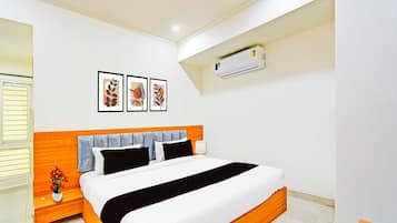 Quarto moderno com cabeceira de madeira, cama grande com roupa de cama preta e branca, mesa de cabeceira com um vaso de flores e três quadros na parede.