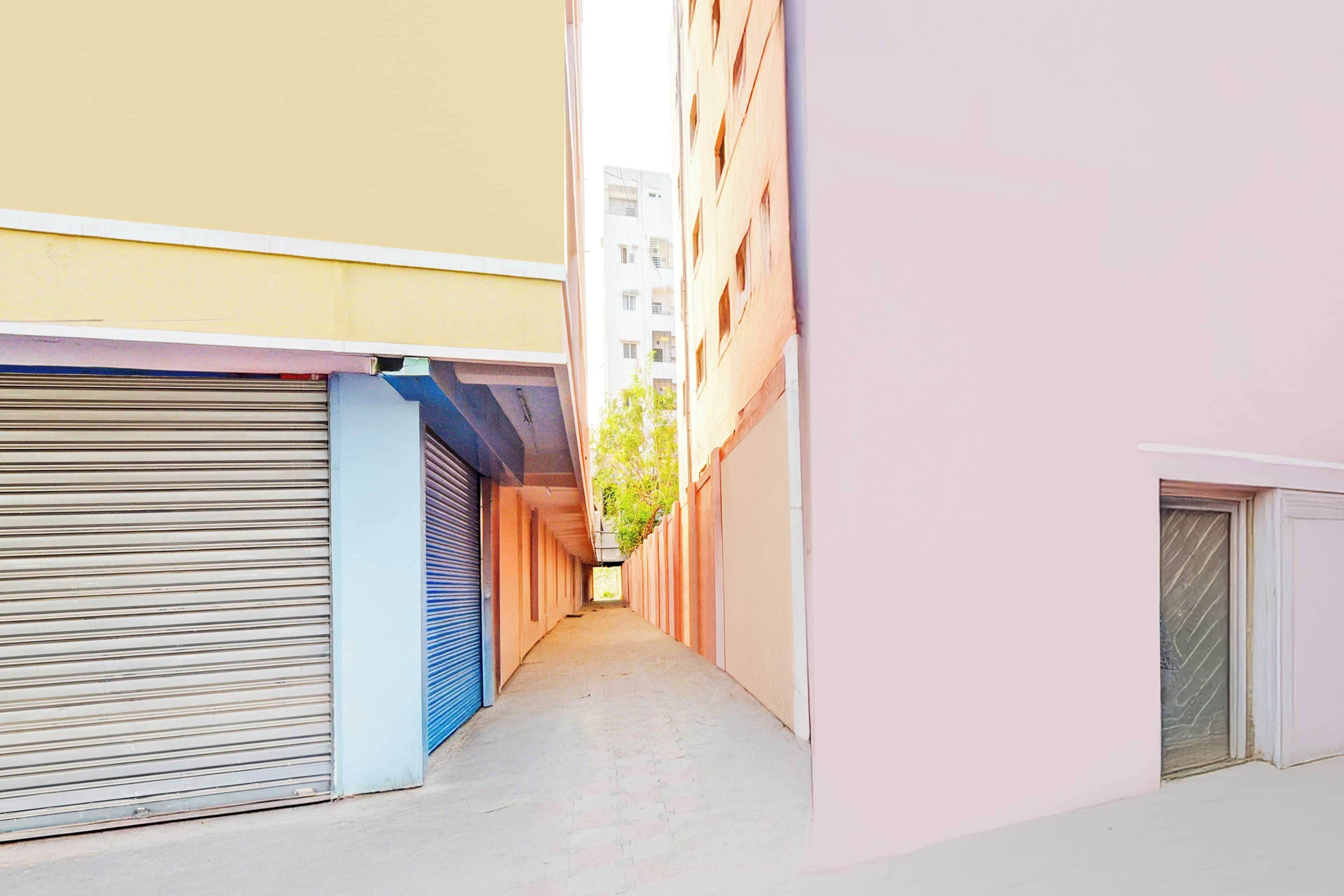 Um beco estreito entre edifícios, com persianas fechadas à esquerda e uma árvore ao centro.