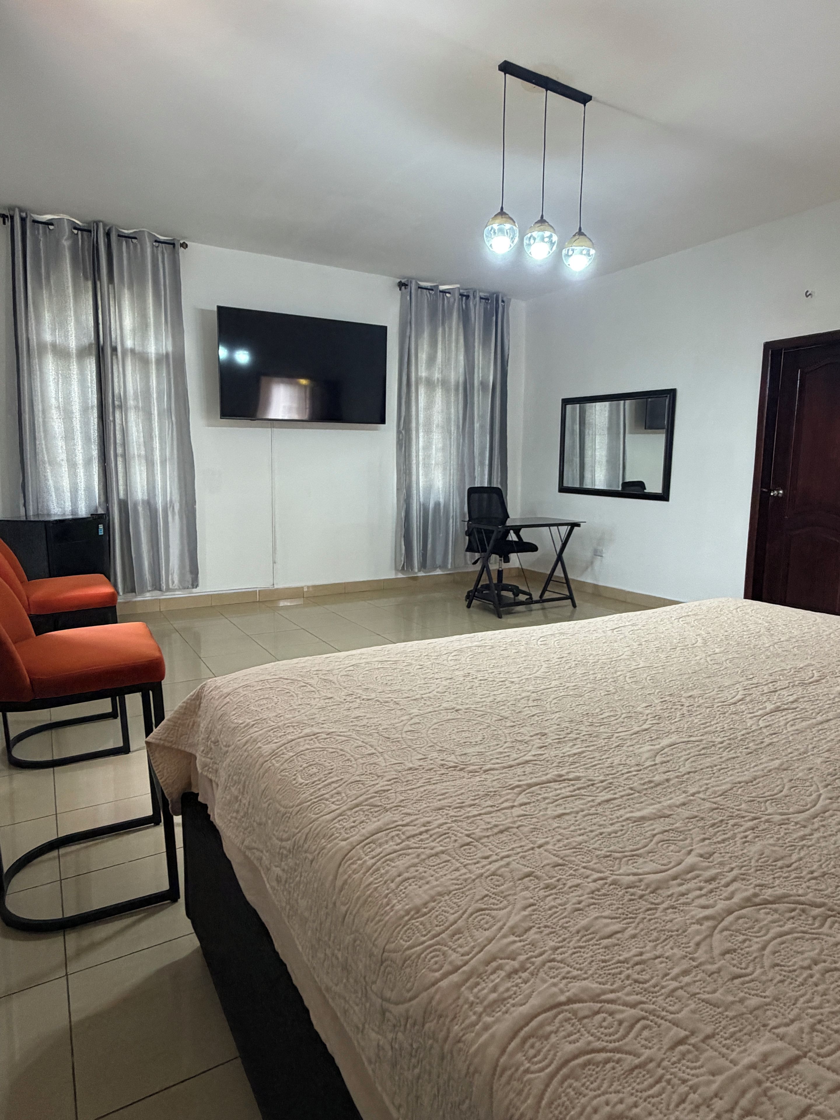 Quarto de hotel com cama, escrivaninha, cadeira, televisão e espelho.