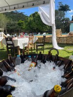 Uma área de refeições ao ar livre com mesas e cadeiras, uma piscina e um bar com garrafas em gelo.