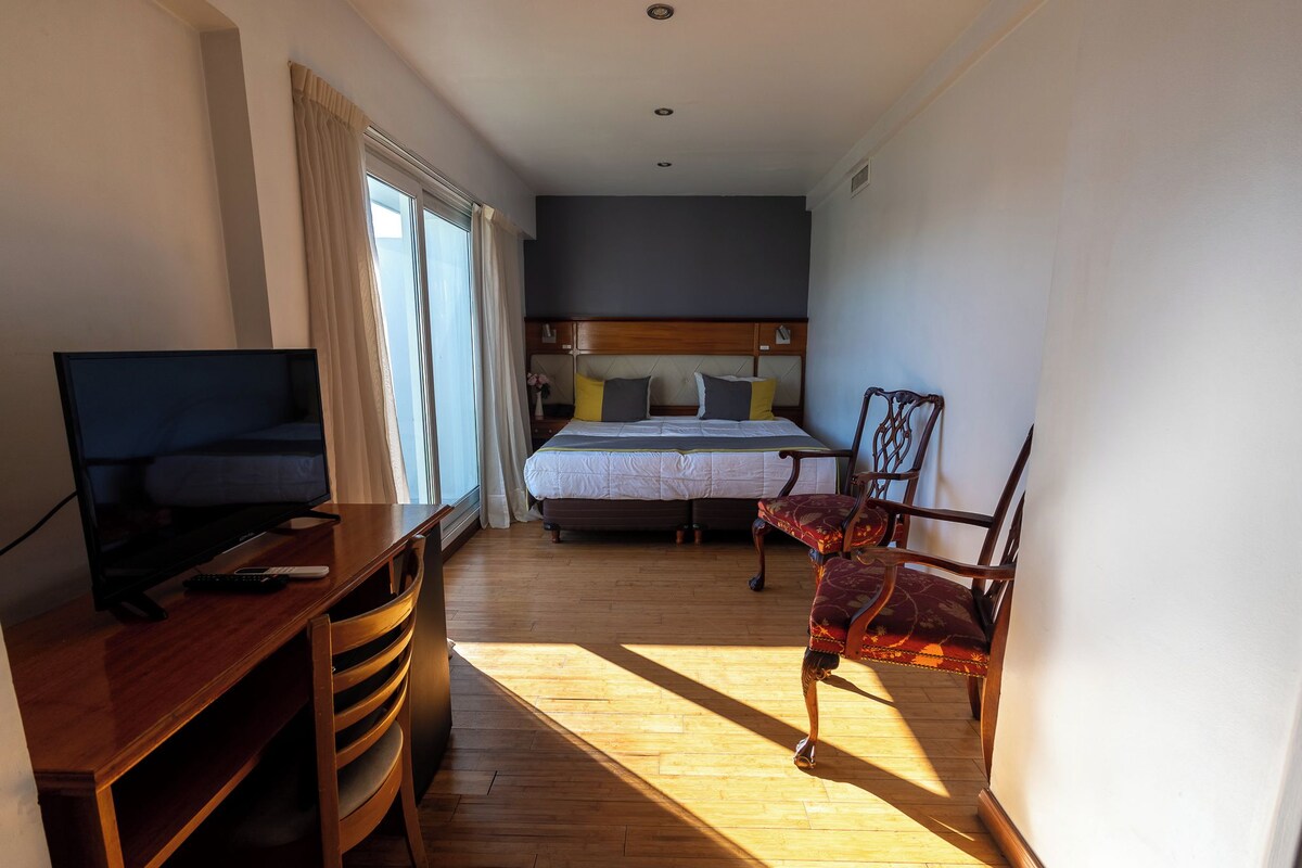 Quarto de hotel com cama, televisão, escrivaninha e cadeira.